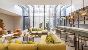 Um interior moderno com sofá amarelo, mesas redondas e um espaço de bar com banquetas.