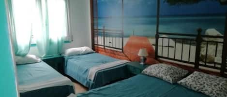 Quarto com duas camas, janela com vista para o mar e abajur na mesinha de cabeceira.