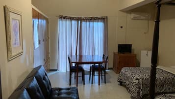 Quarto com sofá de couro preto, mesa de jantar de madeira com cadeiras, cama com padrão de zebra e televisão em um armário de madeira.
