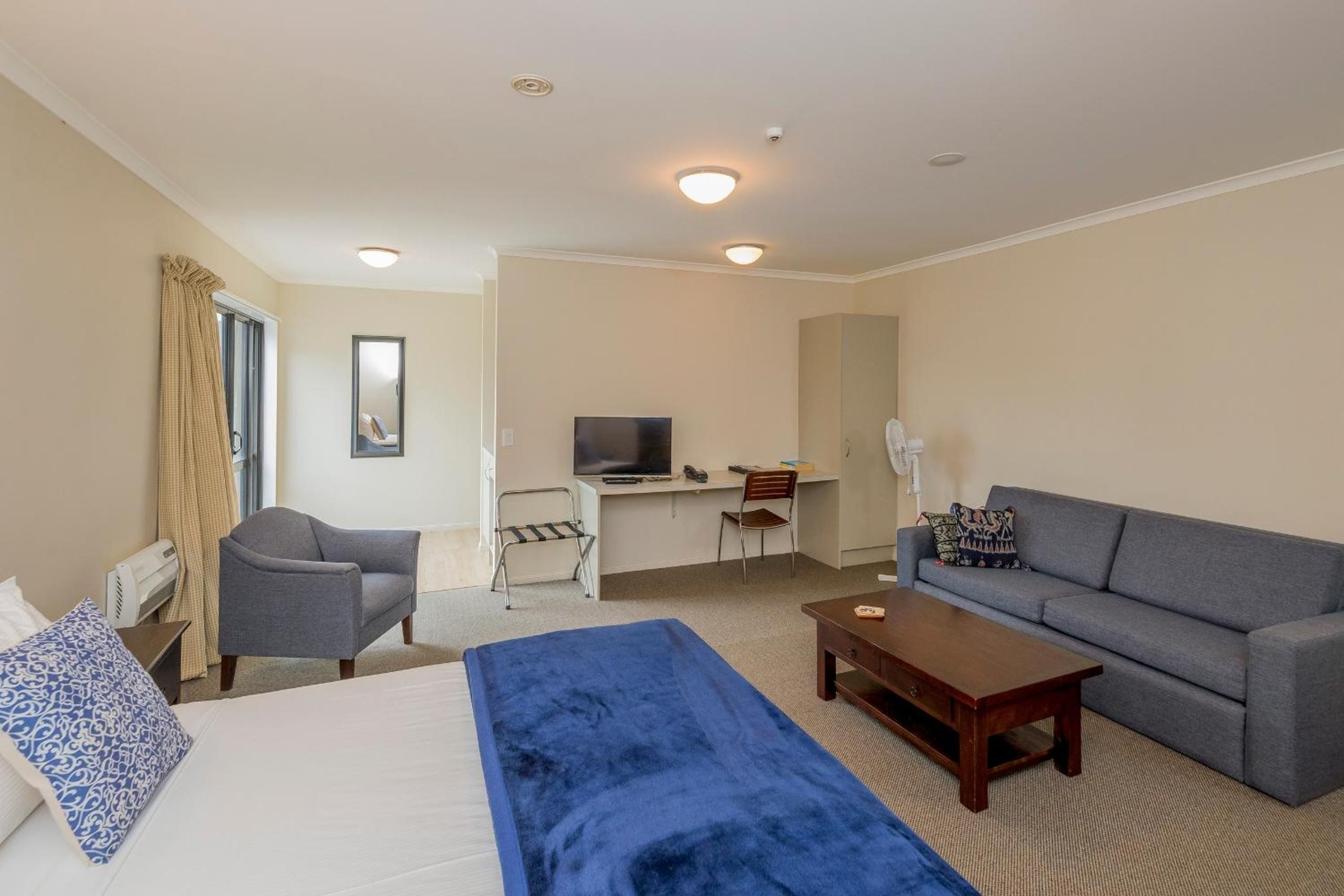 Quarto de hotel com uma cama, um sofá, uma escrivaninha com um computador e uma televisão.