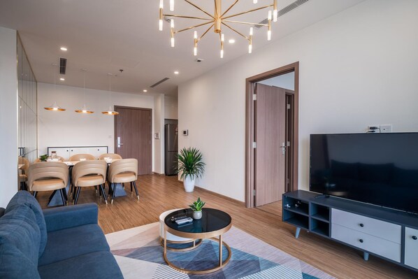 Uma sala de estar moderna com sofá, mesa de centro redonda, painel para TV e um espaço de jantar com cadeiras e mesa.