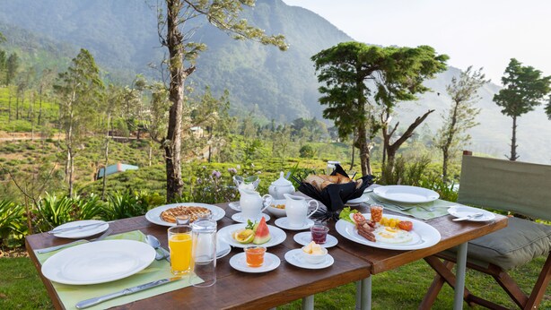 Mesa posta para o café da manhã, com vista panorâmica das montanhas ao fundo.