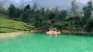 Uma piscina com água cristalina, rodeada por vegetação exuberante e montanhas ao fundo.