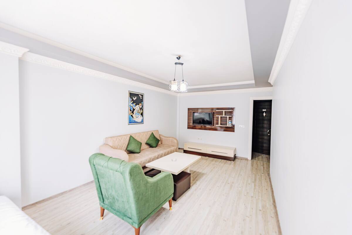 Uma sala de estar moderna com uma poltrona verde, sofá bege e mesa de centro branca.
