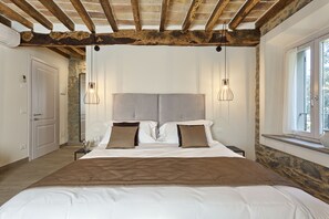 Quarto com uma cama grande, paredes de pedra, teto de madeira e janela com cortinas.