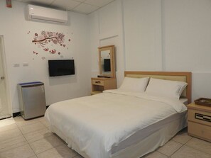 Quarto de hotel com cama, televisão, espelho, pequena escrivaninha e frigorífico.