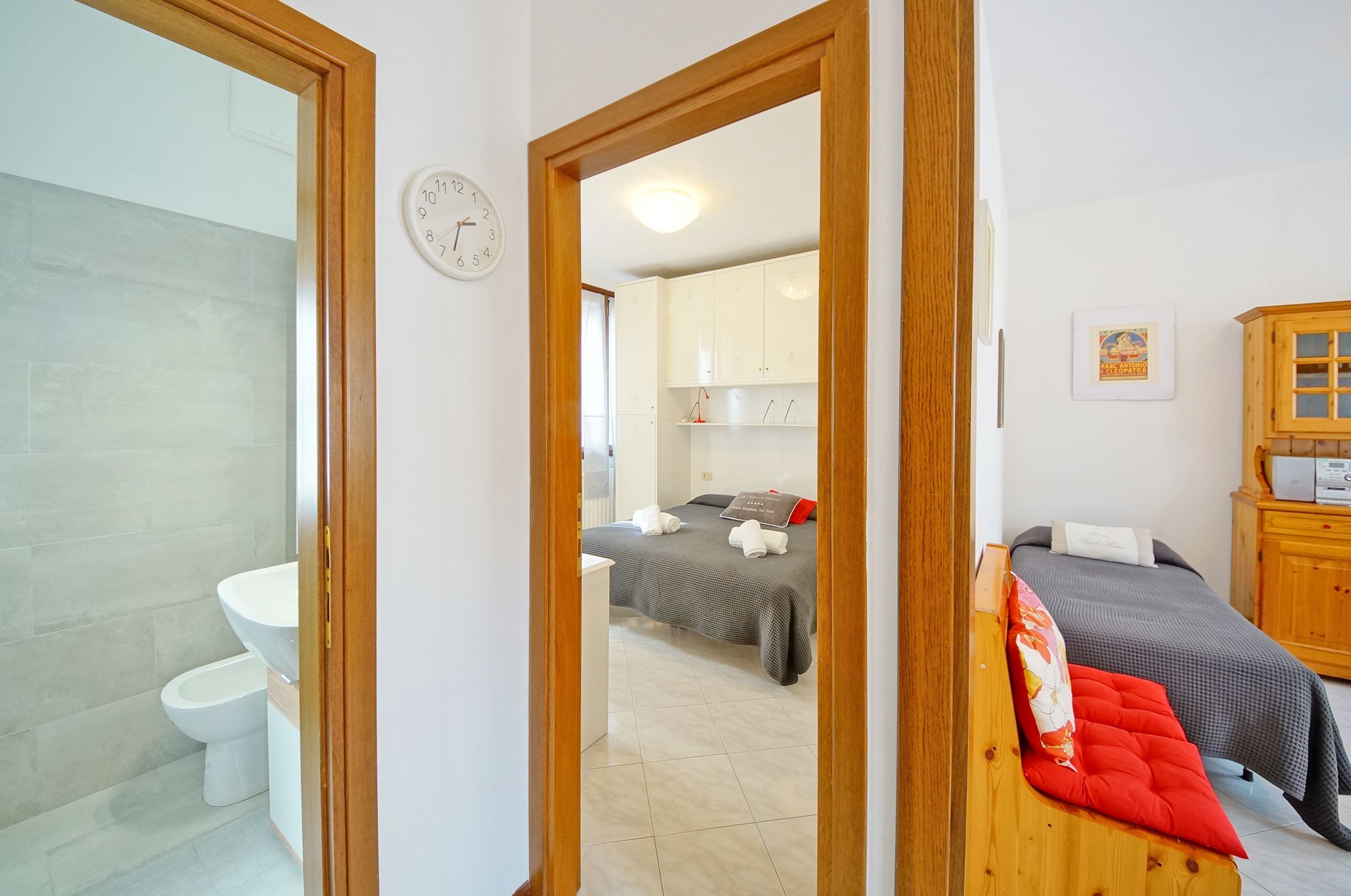 Quarto de hotel com banheiro, uma cama com travesseiro vermelho e um armário de madeira.