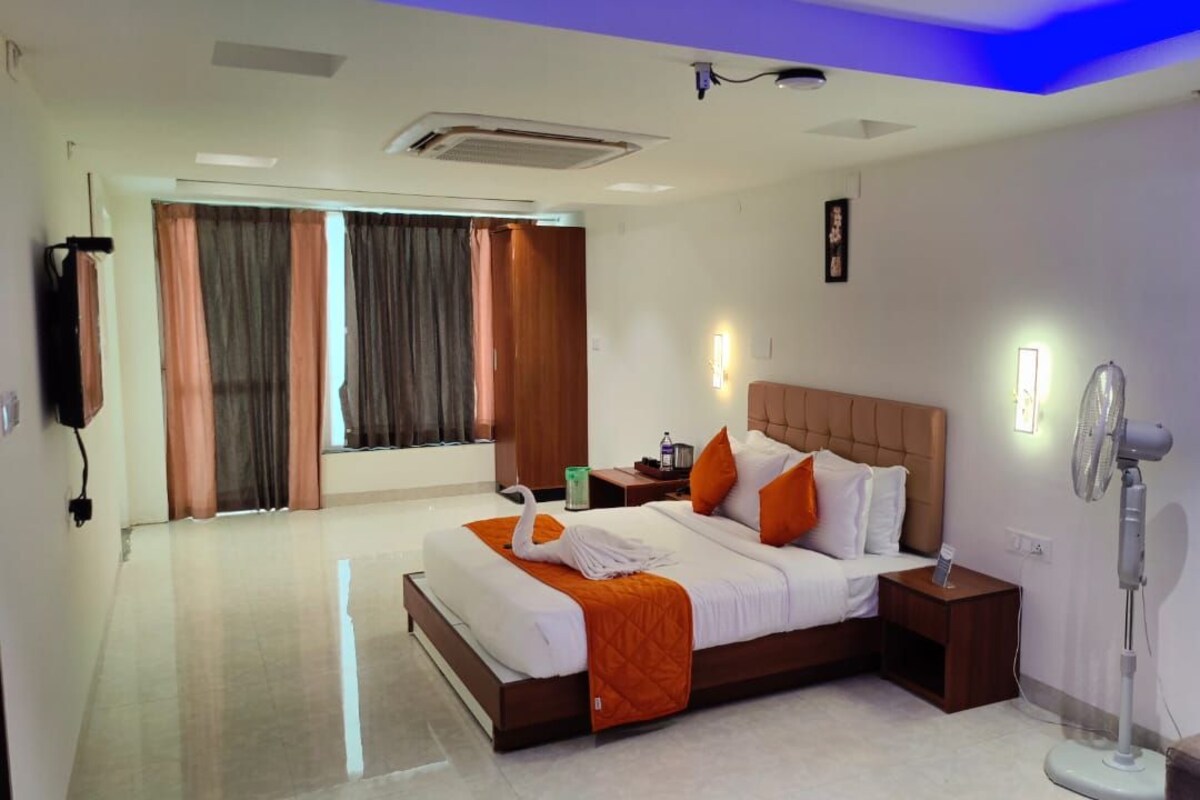 Quarto de hotel moderno com uma cama grande, mesas de cabeceira, um ventilador e uma janela com cortinas.