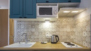 Cozinha com armários verde-água, micro-ondas, pia, chaleira e painel de fundo estampado.