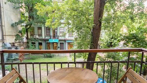 Uma varanda com mesa de madeira e duas cadeiras, com vista para um jardim e edifícios.