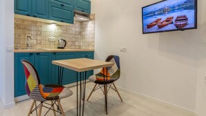 Cozinha moderna com armários verde-água, uma mesa de madeira e duas cadeiras coloridas. Uma televisão na parede exibe barcos.