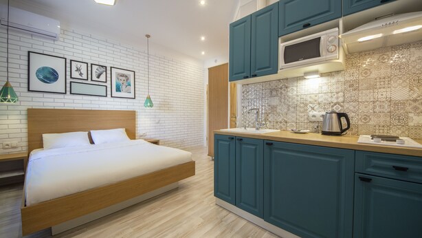Quarto moderno com cama de madeira e cozinha compacta com armários verde-água e micro-ondas.