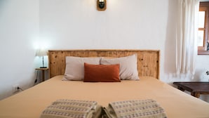 Cama bem arrumada com cabeceira de madeira, duas almofadas e toalhas dobradas sobre a cama.