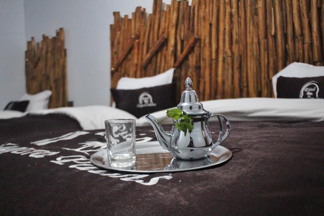 Quarto bem arrumado com uma cama, uma mesa de cabeceira com uma chaleira e um copo, e um painel decorativo na parede.