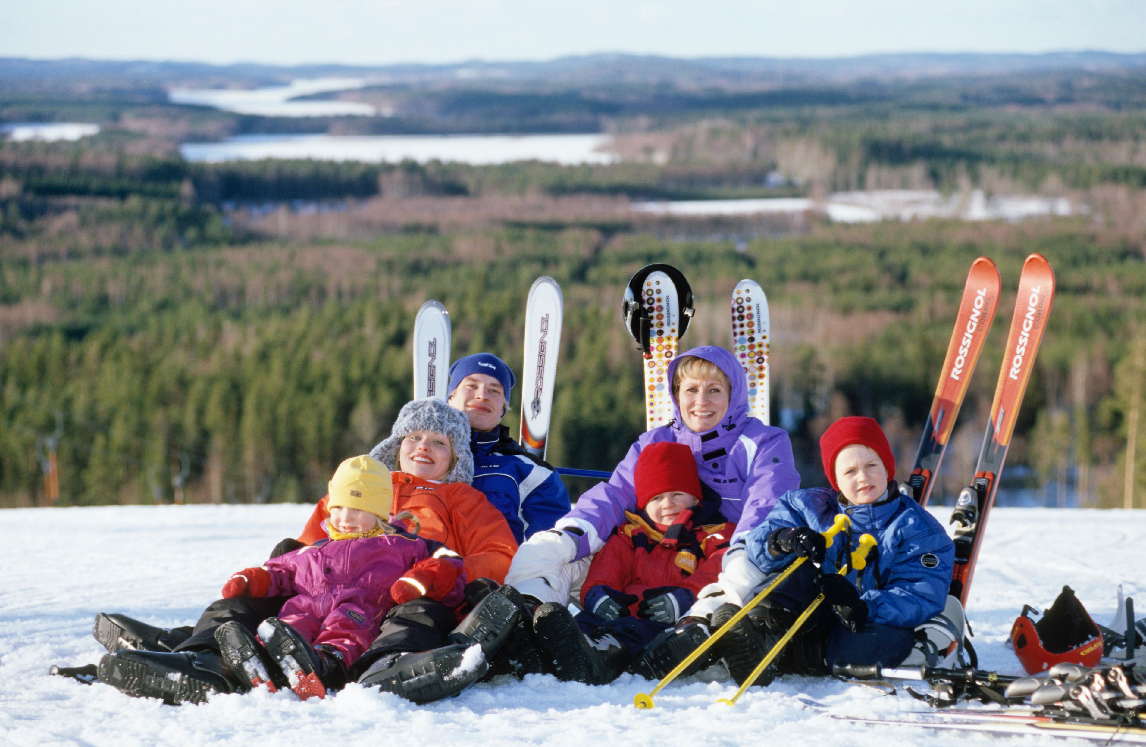 Um grupo de pessoas sentadas na neve, com esquis à frente de uma paisagem arborizada.