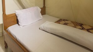 Cama com estrutura de madeira e roupa de cama branca, incluindo um cobertor estampado.