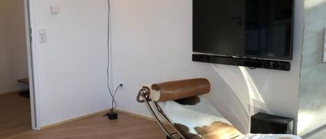 Quarto moderno com piso de madeira, televisão na parede e poltrona de massagem.