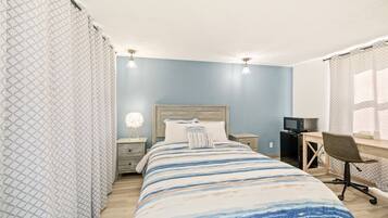 Quarto com cama, escrivaninha, cadeira, televisão e mesa de cabeceira.