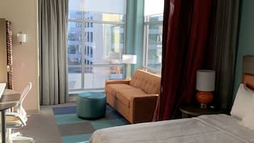 Quarto de hotel com cama grande, sofá, escrivaninha e janela com cortinas.