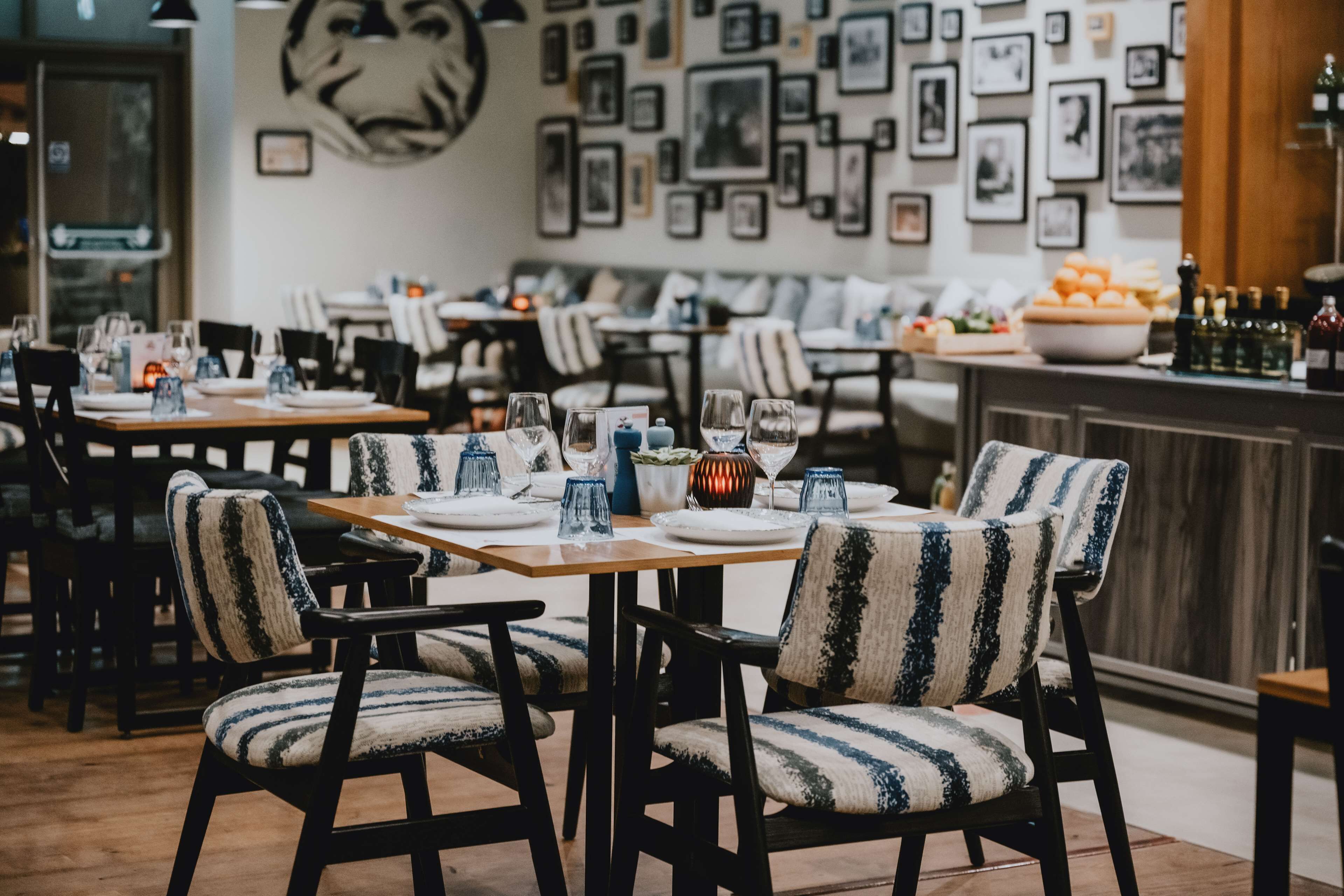 Interior de restaurante com cadeiras listradas, mesas montadas com pratos, copos e um arranjo de velas.