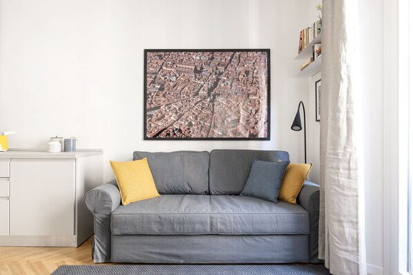 Uma sala de estar moderna com um sofá cinza, uma imagem emoldurada de um horizonte urbano, um armário branco e uma estante.