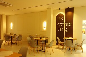 Interior moderno de cafeteria com várias mesas e cadeiras, um letreiro chamativo com a frase 'it's coffee time' e iluminação acolhedora.