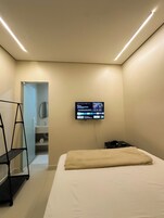 Quarto moderno com cama, televisão na parede, guarda-roupa e espelho.
