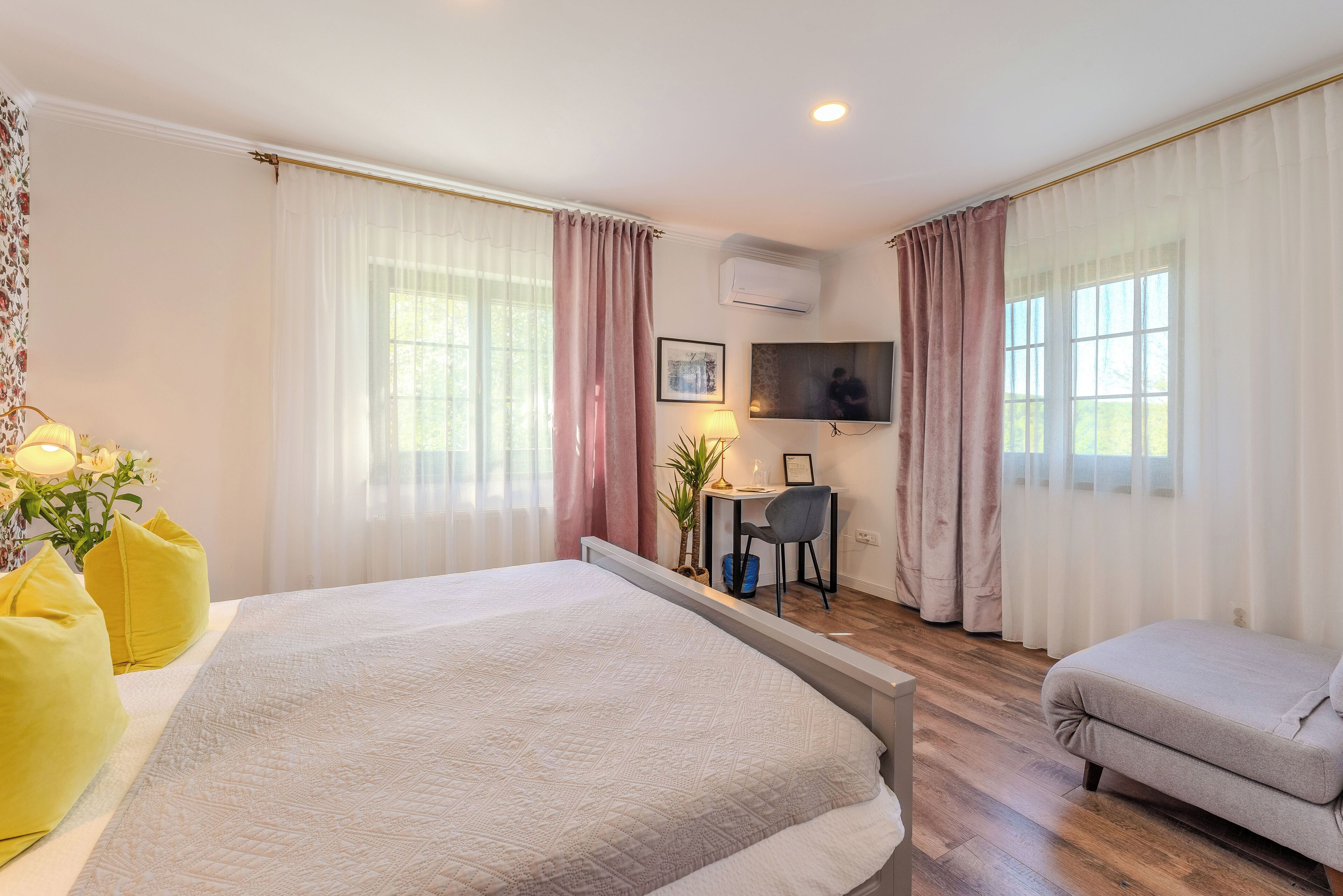 Quarto de hotel com uma cama grande, uma escrivaninha pequena com cadeira, televisão e um sofá.