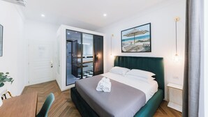 Quarto de hotel moderno com uma cama grande, uma escrivaninha e vista para a praia pela janela.