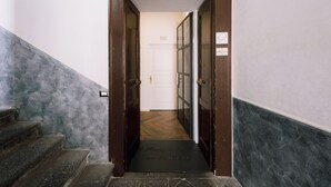 Um corredor com porta de madeira, escadas e parede de mármore.