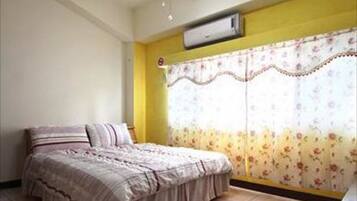 Quarto com cama, ar condicionado e janela com cortinas florais.