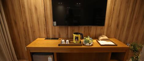 Uma mesa de madeira com uma televisão de tela plana, uma chaleira, uma pequena planta e uma bandeja com um bule e xícaras.