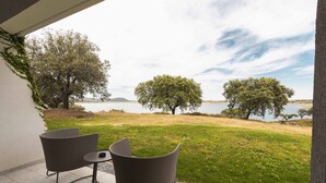 Uma área de estar ao ar livre com duas cadeiras e uma mesa, com vista para uma paisagem gramada e um corpo d'água.