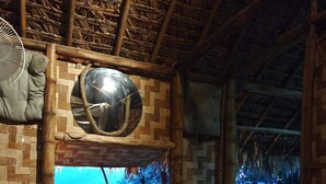 Quarto com teto de bambu trançado, um espelho grande e janela com vista para a água azul.