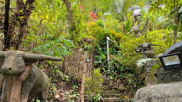 Um caminho de jardim com escadaria de pedra, rodeado por vegetação exuberante e uma estátua decorativa de um touro.