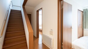 Escada de madeira que leva a um quarto com cama, radiador e porta.