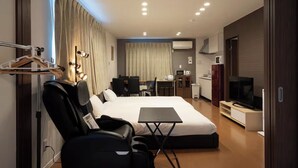 Quarto de hotel moderno com cama, escrivaninha, televisão e cozinha compacta.
