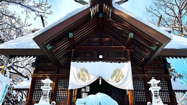 Um edifício de madeira tradicional com telhado coberto de neve e entrada decorativa.