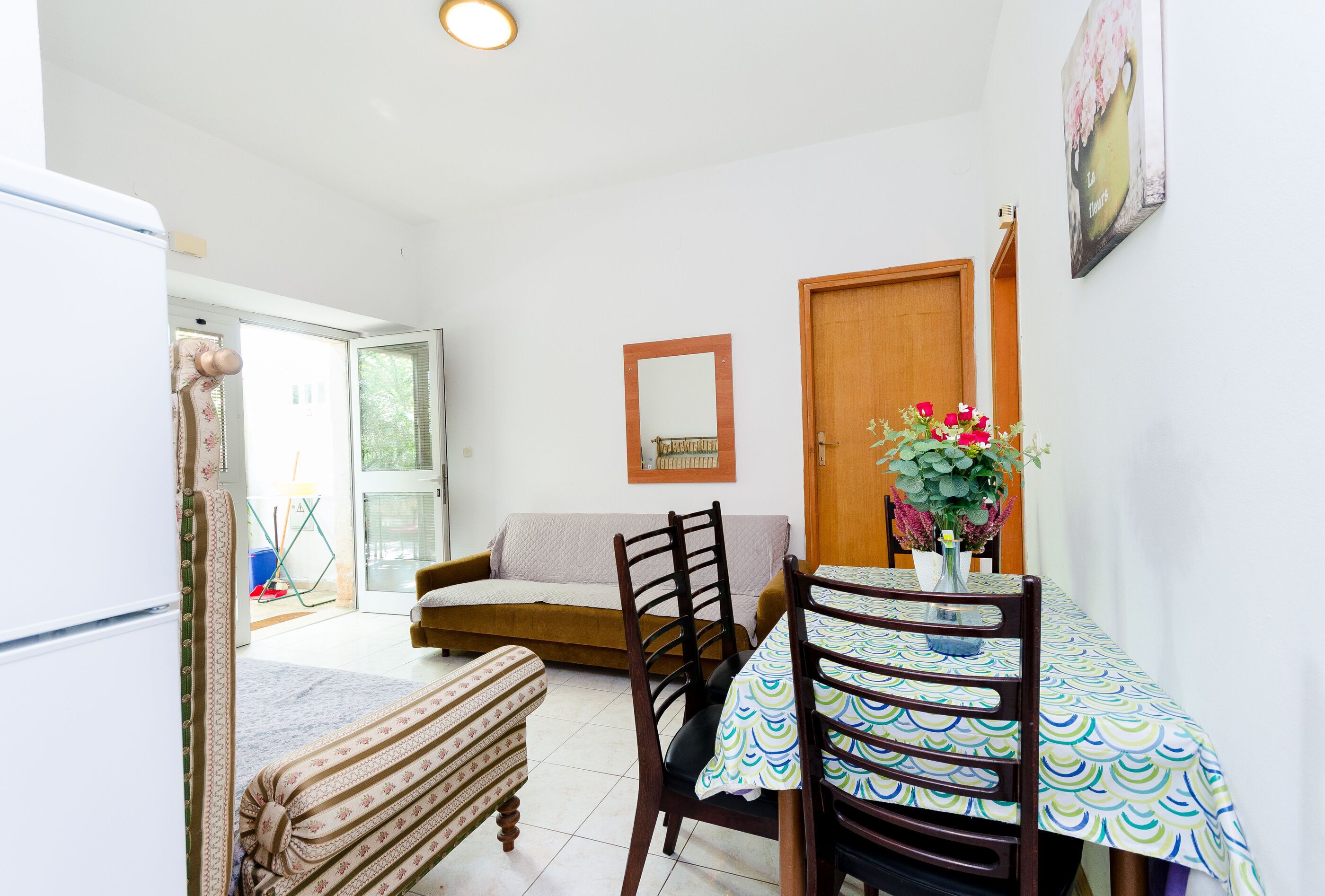Uma sala de jantar com mesa posta para quatro pessoas, um sofá e uma porta de madeira.