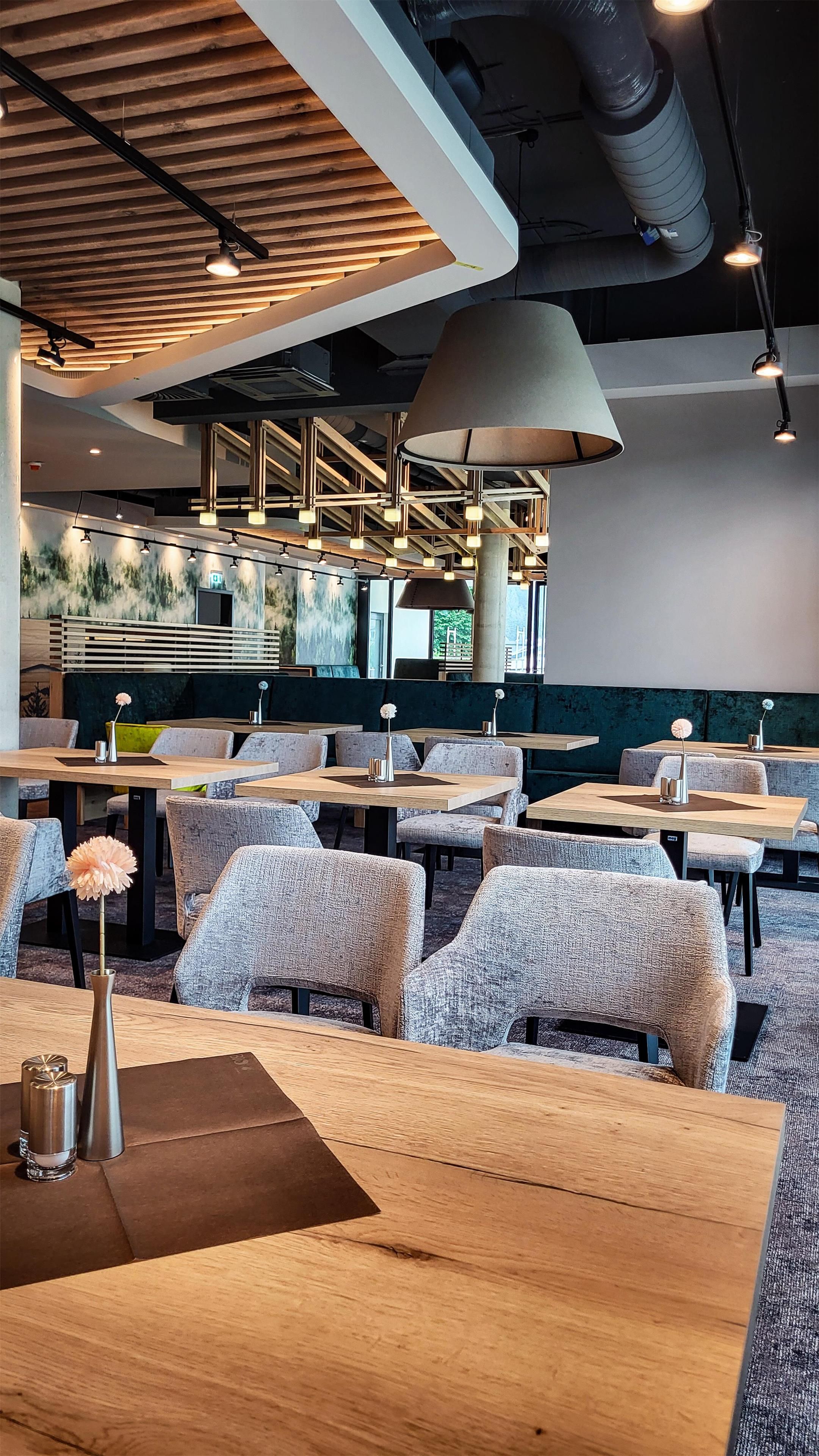Interior de restaurante com várias mesas e cadeiras, uma luminária pendente grande e um mural na parede.
