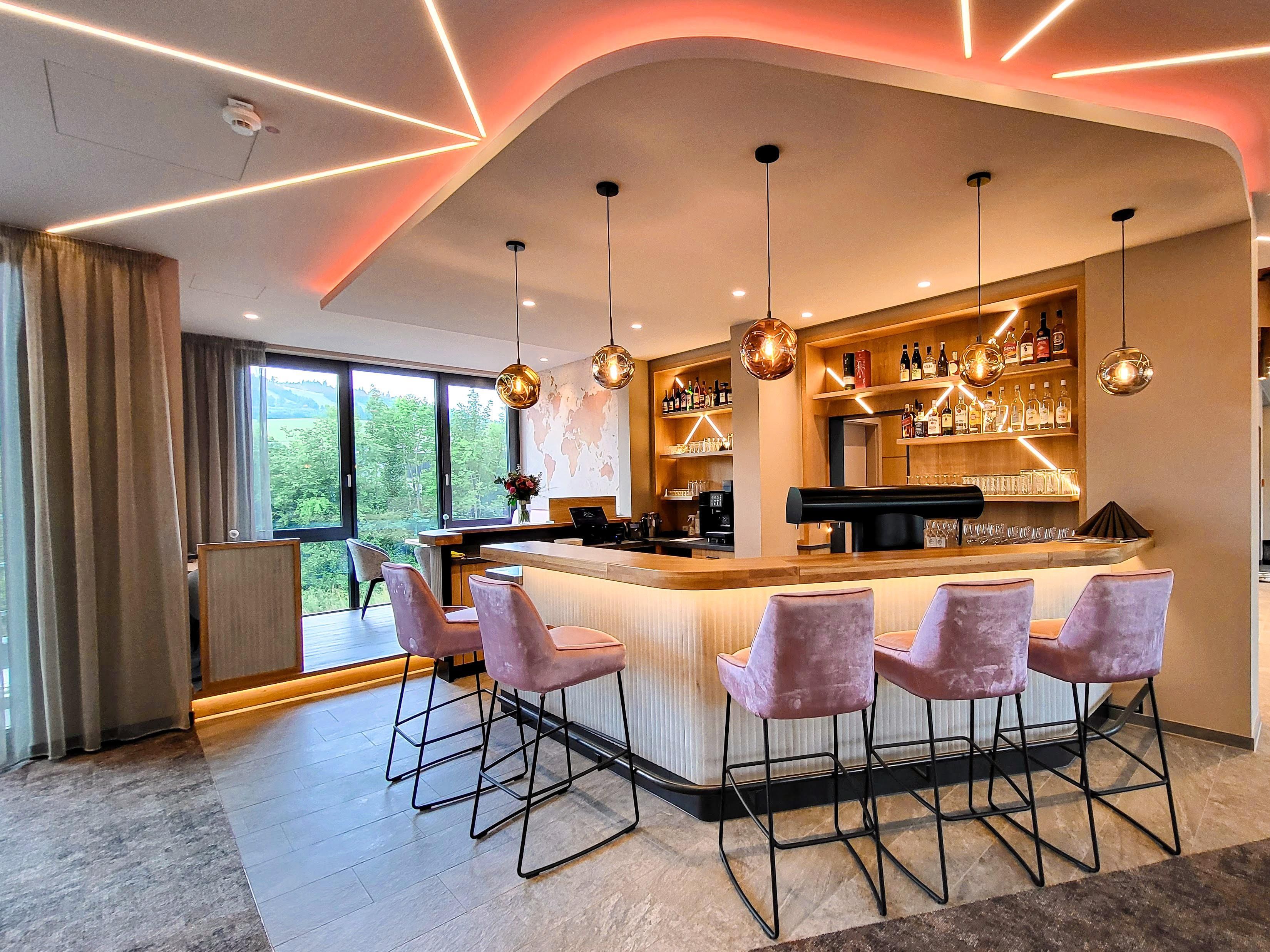 Cozinha moderna com área de bar, banquetas, iluminação pendente e vista para o exterior.