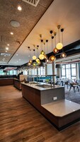 Interior moderno de restaurante com ilha central, várias luminárias pendentes e piso de madeira.
