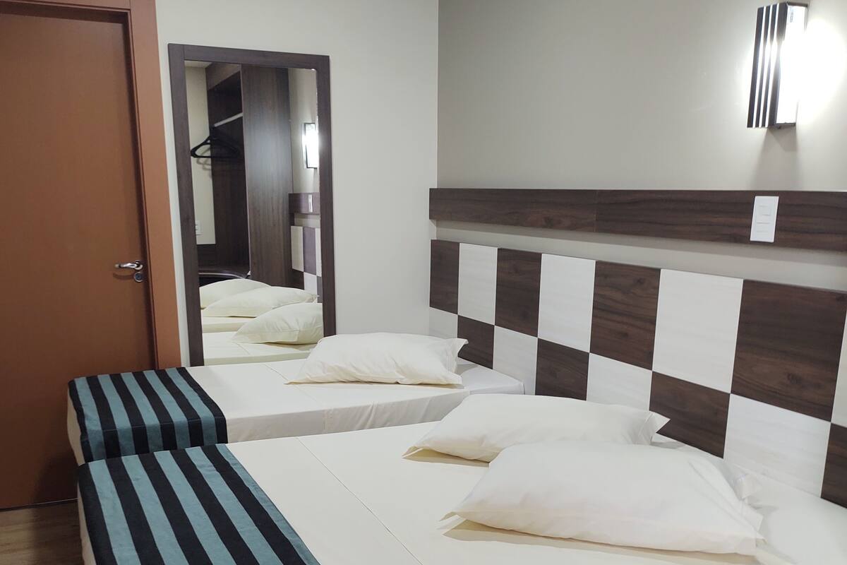 Quarto de hotel com duas camas, piso de madeira, espelho e luminária na parede.