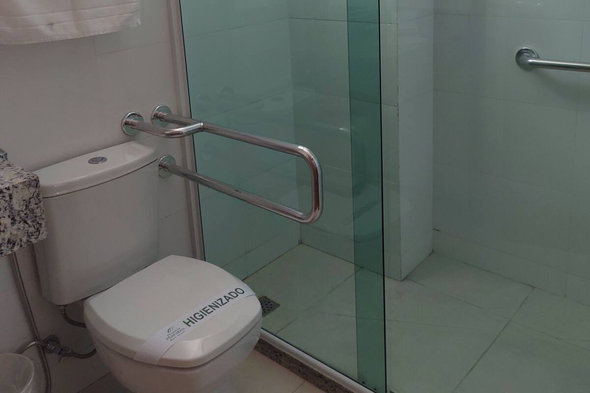 Casa de banho com cabine de chuveiro em vidro, sanita branca e barra para toalhas.