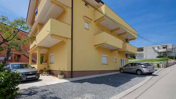 Um edifício residencial amarelo de vários andares com varandas, um carro estacionado em frente e um céu azul límpido.
