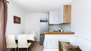 Um espaço de estar compacto com cozinha compacta, área de jantar com mesa e cadeiras, e sofá branco com almofadas.