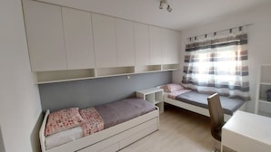 Quarto com duas camas de solteiro, uma escrivaninha e armários embutidos.