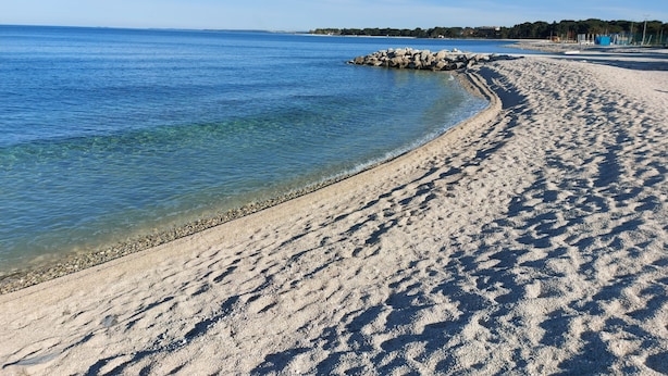 Uma praia de areia com águas cristalinas e um afloramento rochoso ao longe.