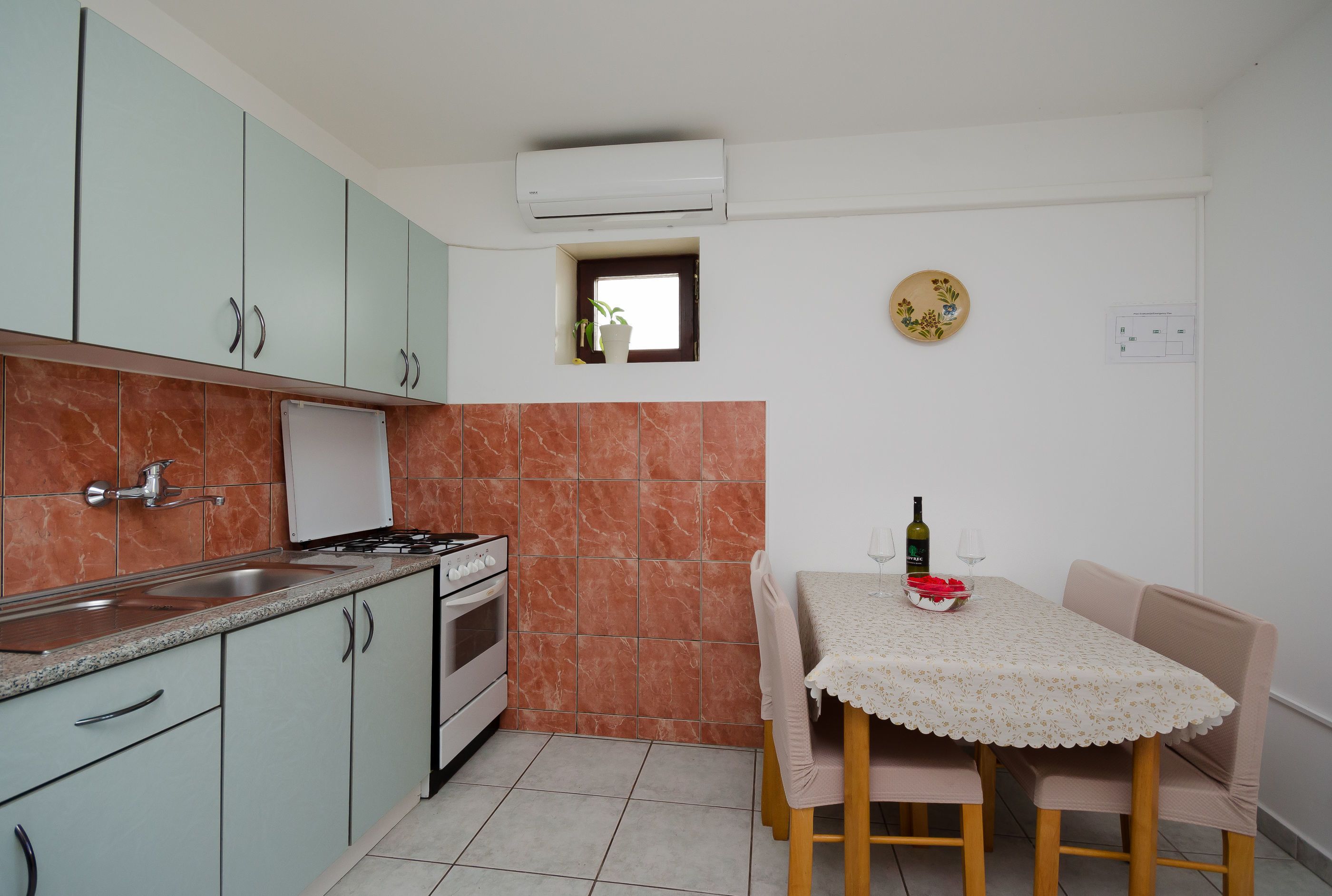 Cozinha compacta com armários verde claro, fogão branco e uma pequena janela com uma planta.