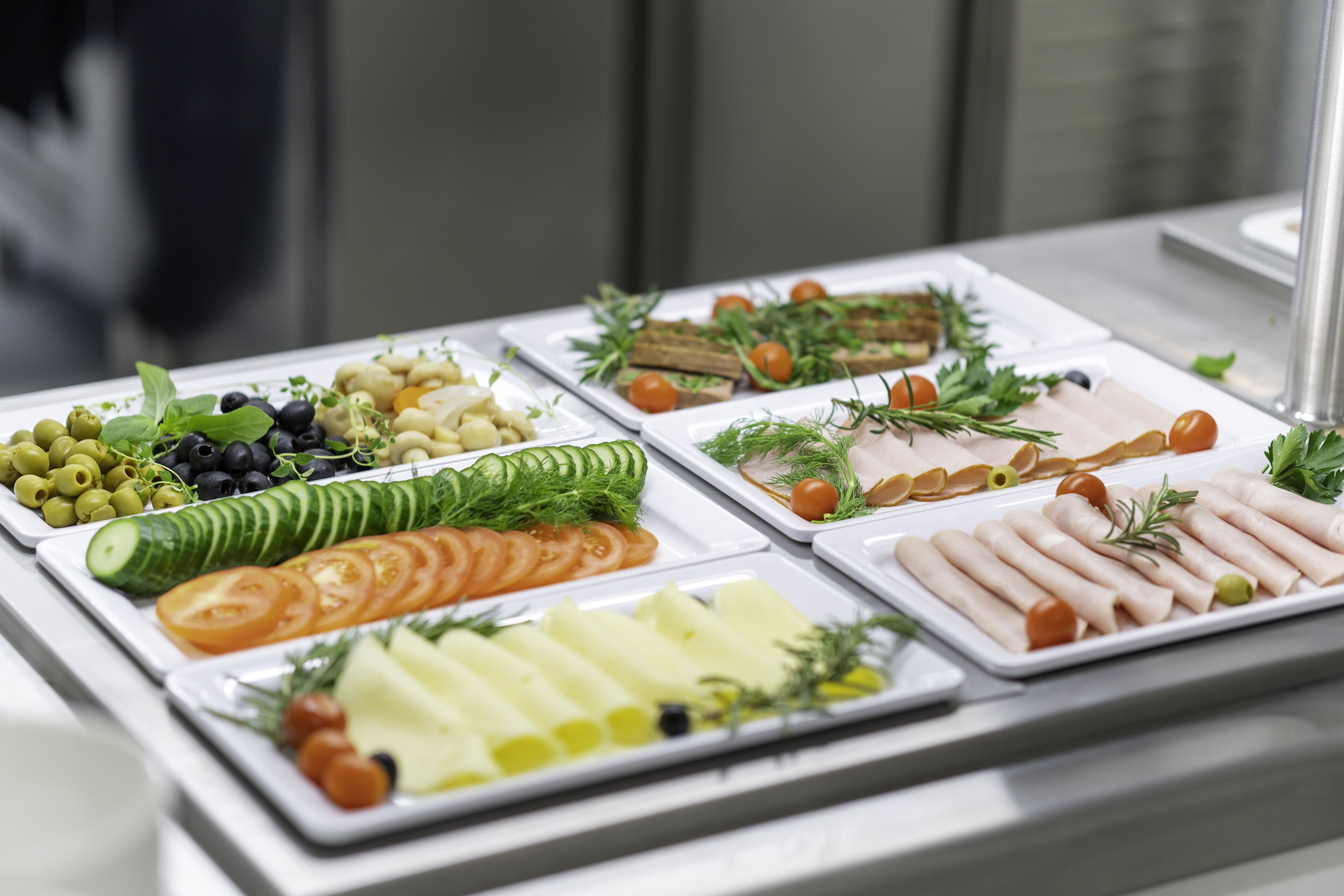 Buffet com diversos alimentos, incluindo pepino fatiado, tomate, queijo e carnes.